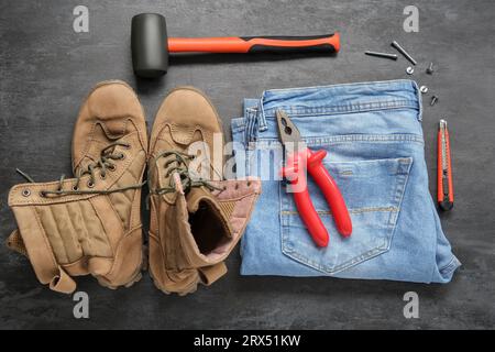 Pair of work boots, jeans and pliers on black grunge background. Labor ...