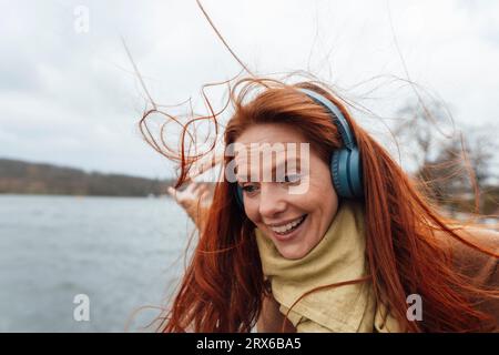 Happy woman with tousled hair listening music on headphones in city ...