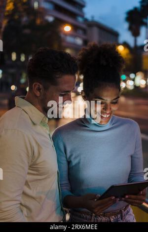 Happy businessman using tablet computer while leaning on desk in office ...