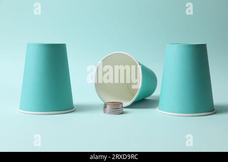 Three paper cups and coins on light blue background. Thimblerig game ...