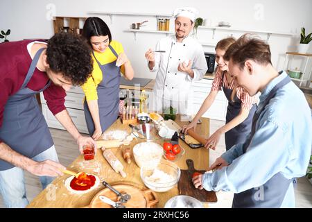 Italian chef with group of young people preparing pizza during cooking ...
