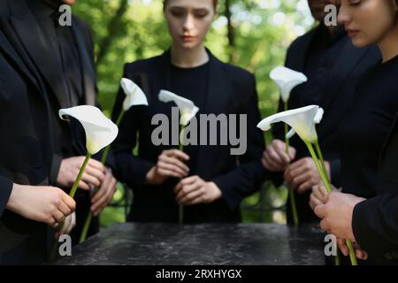 People with calla lily flowers near granite tombstone at cemetery ...