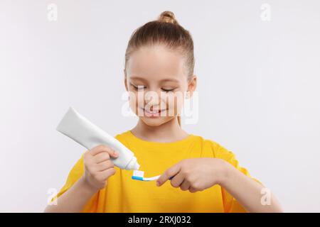 Happy girl squeezing toothpaste from tube onto toothbrush on white ...