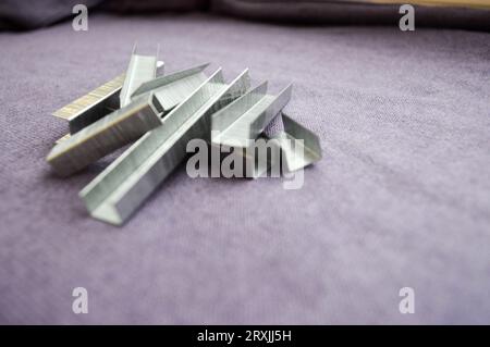 Iron, metal, silvery construction staples stacked in heap on a purple ...