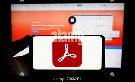 Person holding cellphone with logo of PDF management software Adobe ...