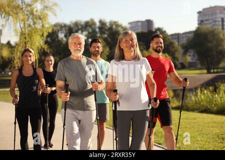 Group of happy people practicing Nordic walking with poles outdoors on ...