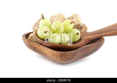 Green ripe gooseberries next to brown cane sugar cubes in wooden bowl ...