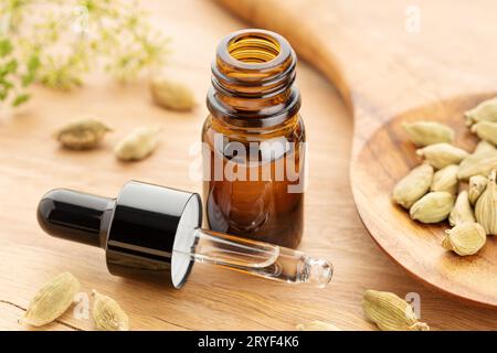 A bottle of aromatherapy essential oil with cardamom seeds on white ...