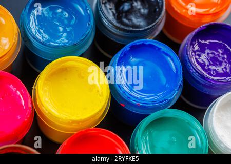 close-up background of opened small gouache paint jars on black surface ...
