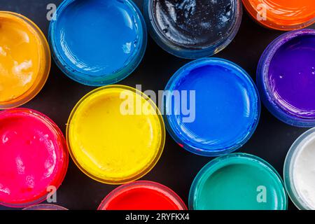 close-up background of opened small gouache paint jars on black surface ...