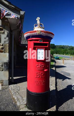 A free-standing letter box with a knitted top, beside a red telephone ...