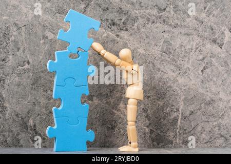 Wooden dummy building a tower from a blue puzzle Stock Photo - Alamy