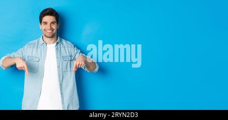 Handsome smiling adult man introduce product, pointing fingers down at ...