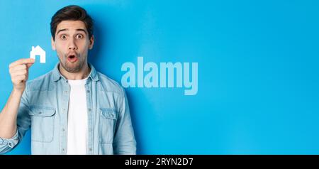 Real estate concept. Surprised guy showing small paper house model ...