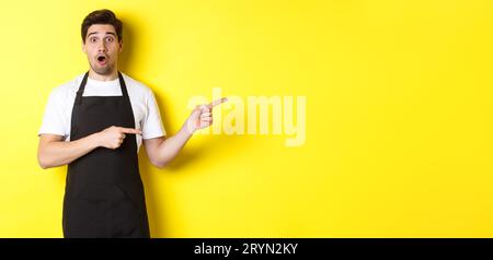 Surprised male waiter in black apron showing logo or advertisement ...