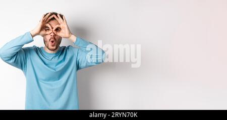 Check it out. Impressed young man seeing awesome promo, looking through ...