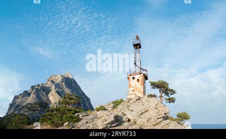 Rock with conifer trees and old lighthouse on slope on blue sky ...