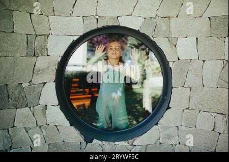 Little girl standing behing round window, looking outside Stock Photo ...