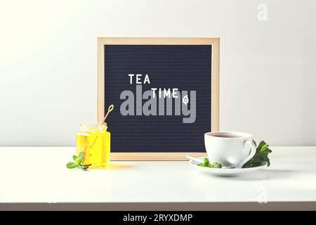 Tea time. Black letter board with text on blue table with glass cup of ...