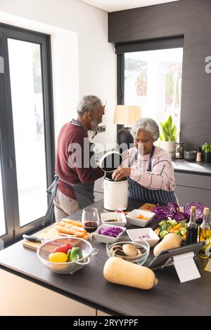 Multiracial senior couple wearing aprons preparing food in kitchen at ...