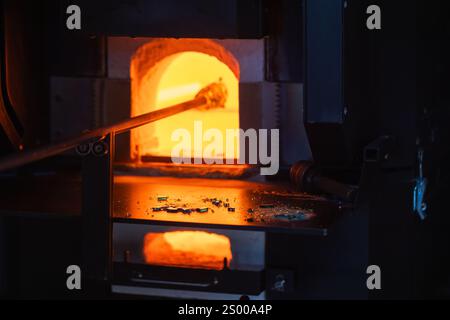 Open furnace with molten glass on a blowpipe inside. Works of glass ...