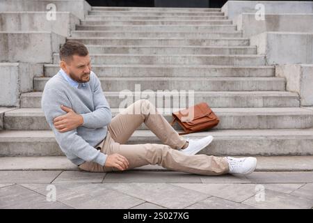 Man with injured arm on stairs outdoors after fall. Dangerous accident ...