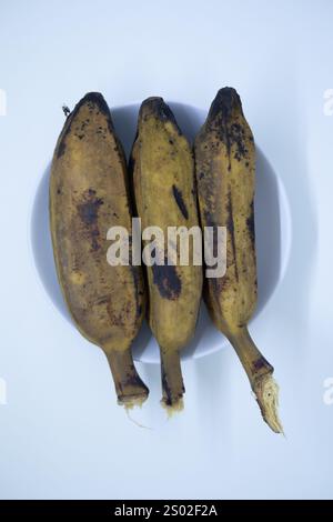 A white plate with ripe bananas and fork with knife on the pink ...