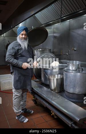 A volunteer in a langar communal kitchen makes rice which will be ...