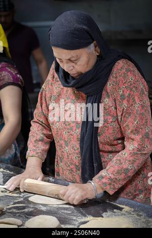 An older Sikh woman rolls dough that will be made into roti bread. Tall ...