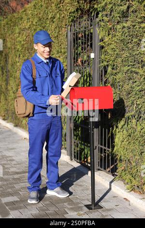 Postman putting parcel into mail box outdoors Stock Photo - Alamy