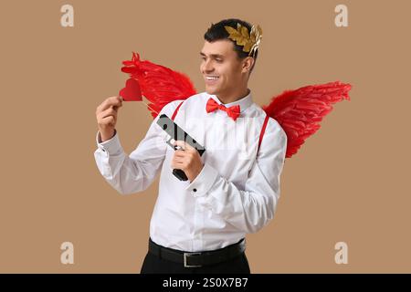 Cool young man dressed as Cupid with gun on beige background. Valentine ...