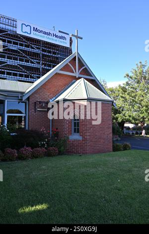 Modest red brick Anglican church overshadowed by large metallic carpark ...