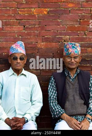 Nepali men, wearing dhaka topi hats, rest under the arches of an old ...