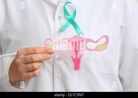 Female doctor with turquoise ribbon holding paper uterus on white ...