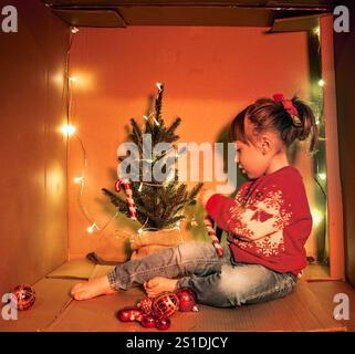 girl in a red Christmas sweater at home next to the Christmas tree ...