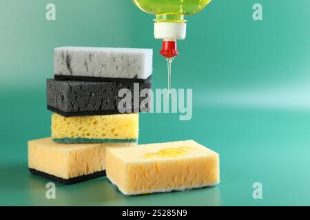 Pouring detergent from bottle onto sponge on green background, closeup ...