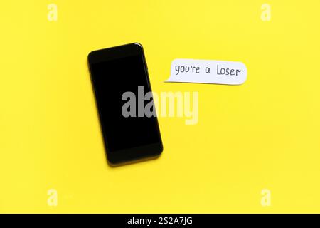 Speech bubble with text YOU'RE LOSER and blank mobile phone on yellow ...