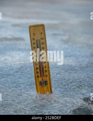 Wooden thermometer stuck in frozen grass displaying freezing ...