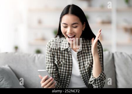 Asian woman using smartphone at home sitting on comfortable sofa ...