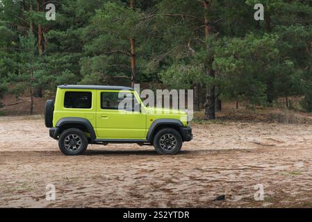 Lime green Suzuki Jimny in pine forest. Three quarter front view of off ...