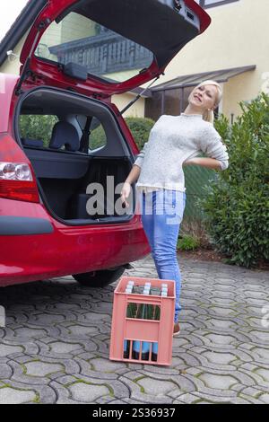 A young woman lifts a crate of bottles out of her car. Proper living ...