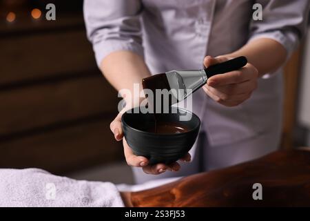 Spa worker with cosmetic product for chocolate body wrap near woman in ...