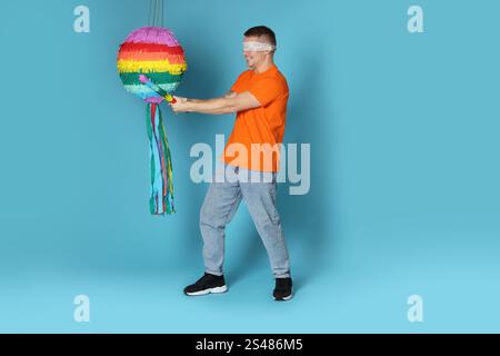 Man with tied eyes breaking pinata on light blue background Stock Photo ...