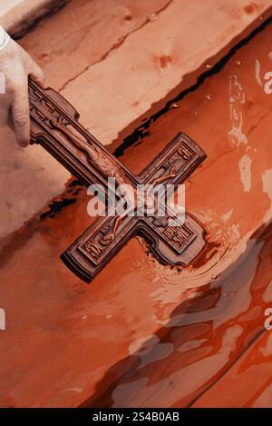Priest consecrating river water for baptism, holy father holding cross crucifix in hand close up ...