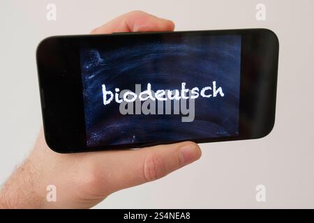 Hand mit Mobiltelefon mit dem Unwort des Jahres 2024 biodeutsch ...