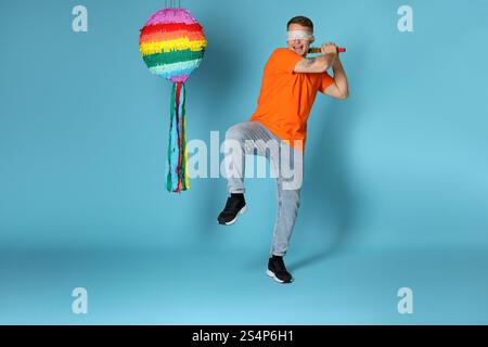 Man with tied eyes breaking pinata on light blue background Stock Photo ...
