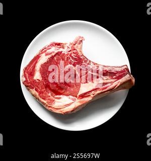 Raw beef prime rib on a plate isolated on black background. Top view ...