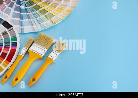 Color selection charts and paint brushes on light blue table, space for ...