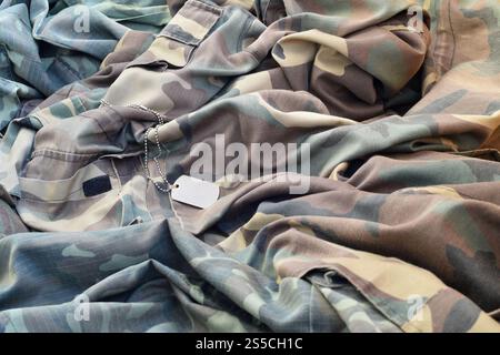 Lost and empty army dog tag lies on pile of folded camouflage clothes ...