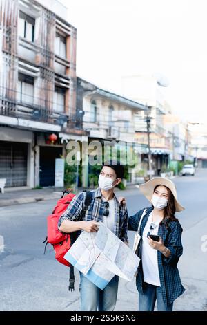 Male tourist wear hat with face mask with backpack use tablet while sit ...